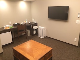 Quarto de hotel com escrivaninha, cadeira, televisão e uma pequena cozinha equipada.