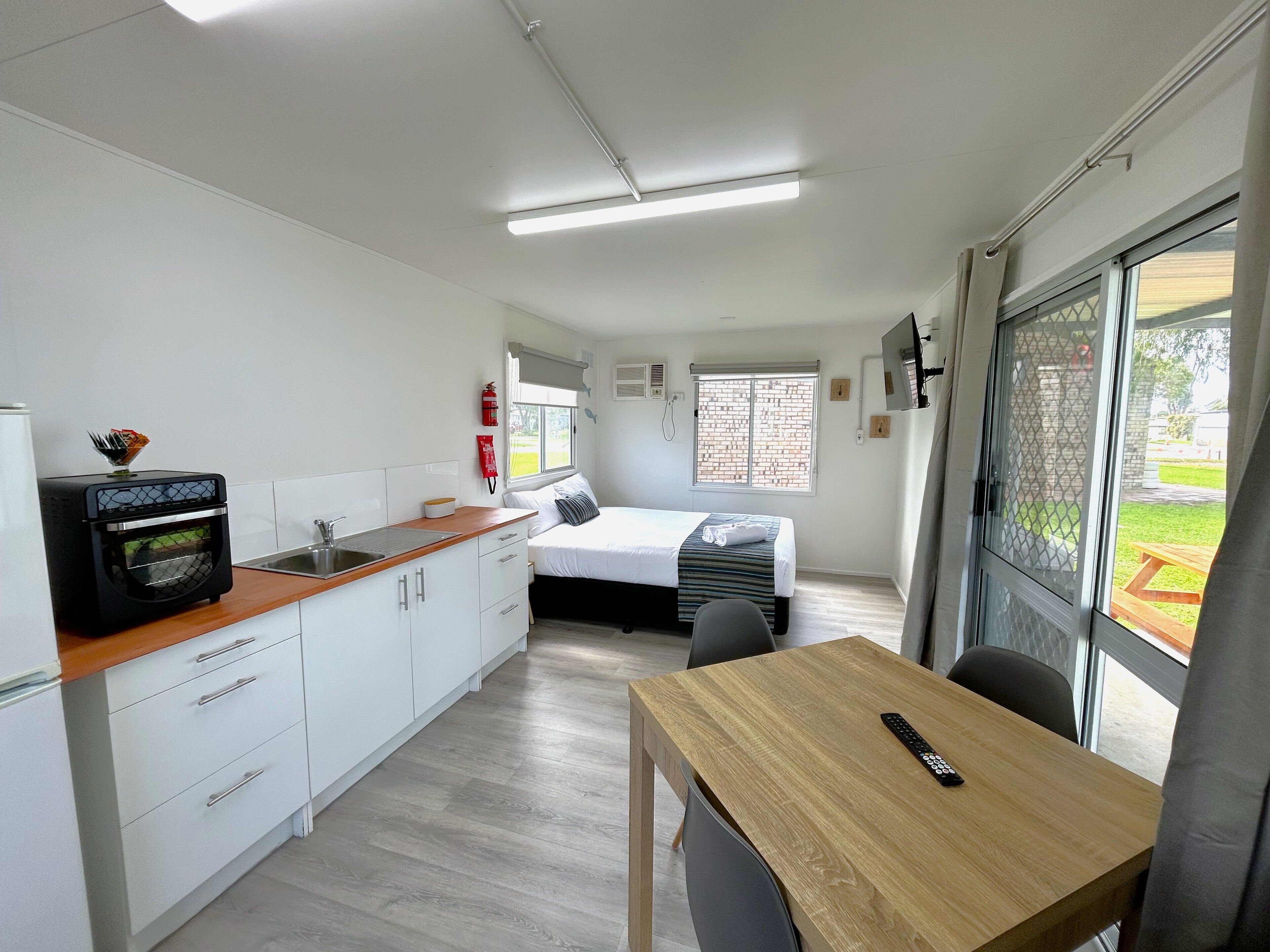 Quarto compacto com cozinha compacta, cama, mesa e janela.