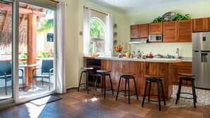 Uma cozinha com ilha central, banquetas, micro-ondas e geladeira.