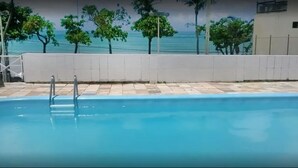 Piscina com deck revestido e um mural com árvores e uma praia ao fundo.