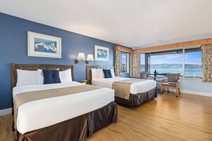 Quarto de hotel com duas camas, uma mesa de jantar e vista para o mar.