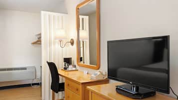 Quarto de hotel com escrivaninha de madeira, espelho, televisão, cadeira, telefone e aquecedor.