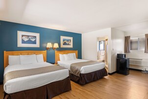 Quarto de hotel com duas camas, cabeceiras de madeira, uma mesa com computador e obras de arte nas paredes.