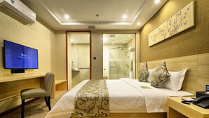 Quarto de hotel com cama grande, televisão, escrivaninha e chuveiro.