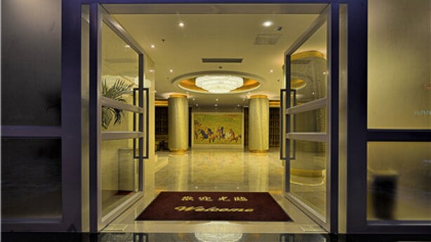 Entrada de hotel com porta de vidro, tapete de boas-vindas e um mural na parede.
