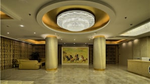 Um hall com um grande candelabro, duas colunas, um balcão de recepção e um mural na parede.