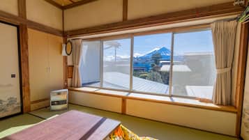 Quarto japonês tradicional com tatames, futon, aquecedor e vista para uma montanha.