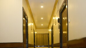 Corredor de hotel com portas em ambos os lados, piso ladrilhado e cortina no final.