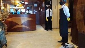 Um saguão de hotel com balcão de recepção, piso de madeira e parede com relógio.