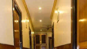 Corredor de hotel com portas de madeira, piso ladrilhado e iluminação embutida.