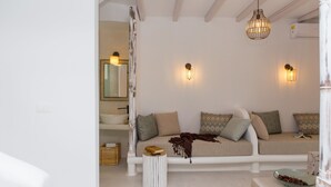 Uma sala de estar moderna com um sofá branco, almofadas decorativas, uma pequena mesa lateral e duas luminárias fixadas na parede.