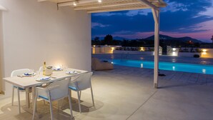 Uma área de refeições ao ar livre com piscina e vista para as montanhas ao entardecer.