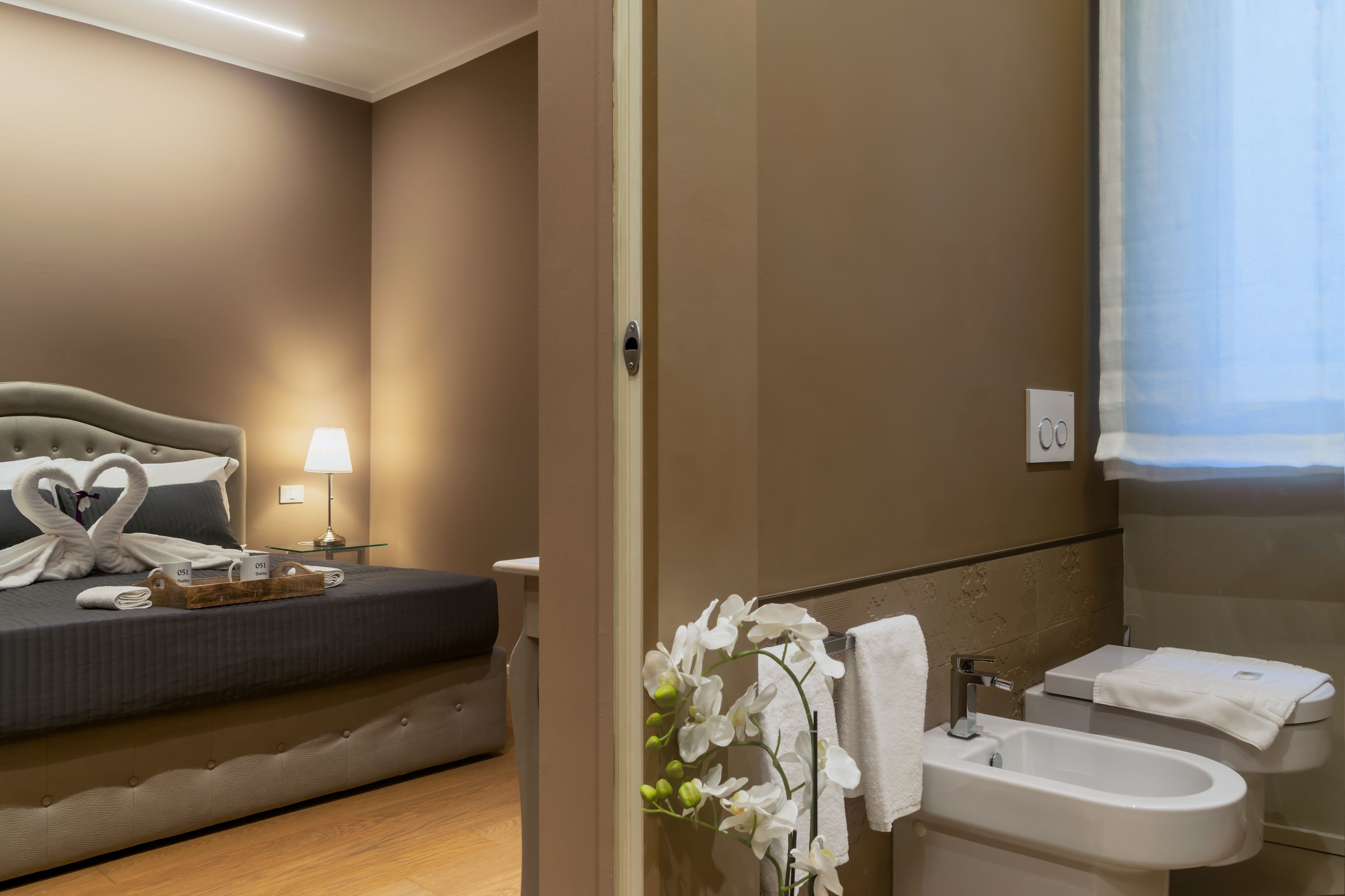 Quarto de hotel com cama, mesa de cabeceira com abajur, banheiro com pia e porta-toalhas.