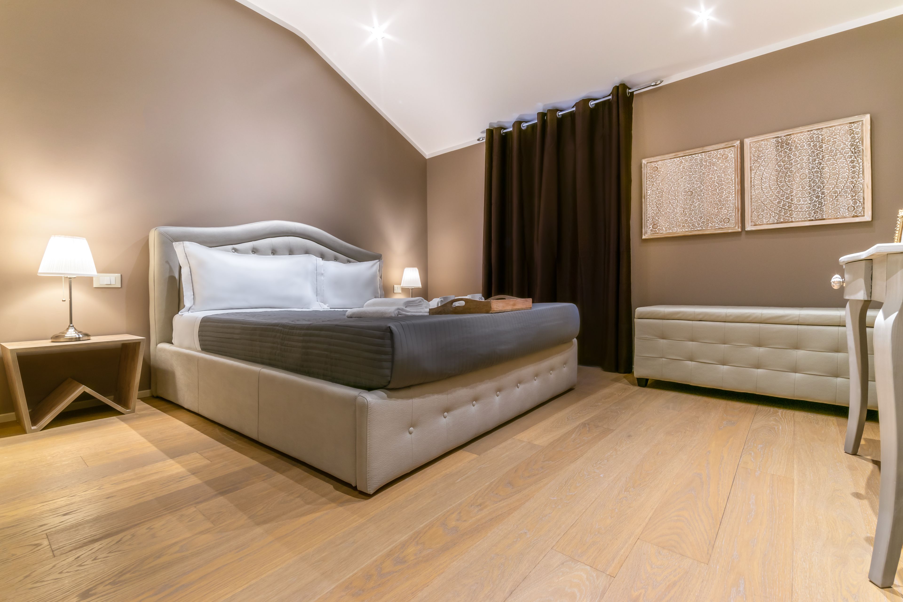 Quarto moderno com uma cama grande, mesa de cabeceira com abajur, cômoda e dois painéis decorativos na parede.