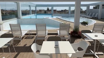 Uma área de piscina no terraço com cadeiras e mesas brancas, vista clara da paisagem urbana e design arquitetônico moderno.
