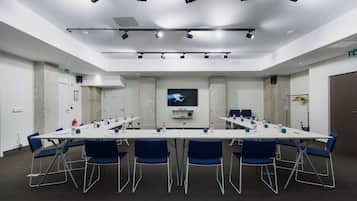 Uma sala de conferências com uma mesa comprida, cadeiras azuis e uma TV de tela plana na parede.