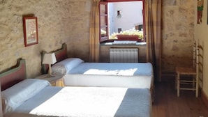 Quarto rústico com duas camas, uma cadeira de madeira e uma janela com cortinas.