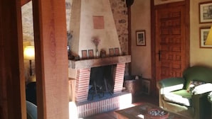 Uma sala de estar acolhedora com lareira de pedra, vigas de madeira e uma poltrona verde.