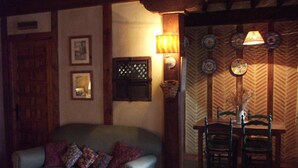 Uma sala de estar acolhedora com um sofá, uma mesa e cadeiras. Há luminárias na parede e pratos decorativos.