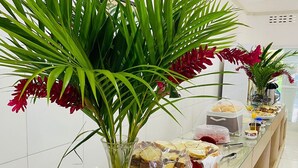 Uma mesa de buffet com diversos alimentos, um vaso de vidro com plantas verdes e um arranjo de flores decorativo.
