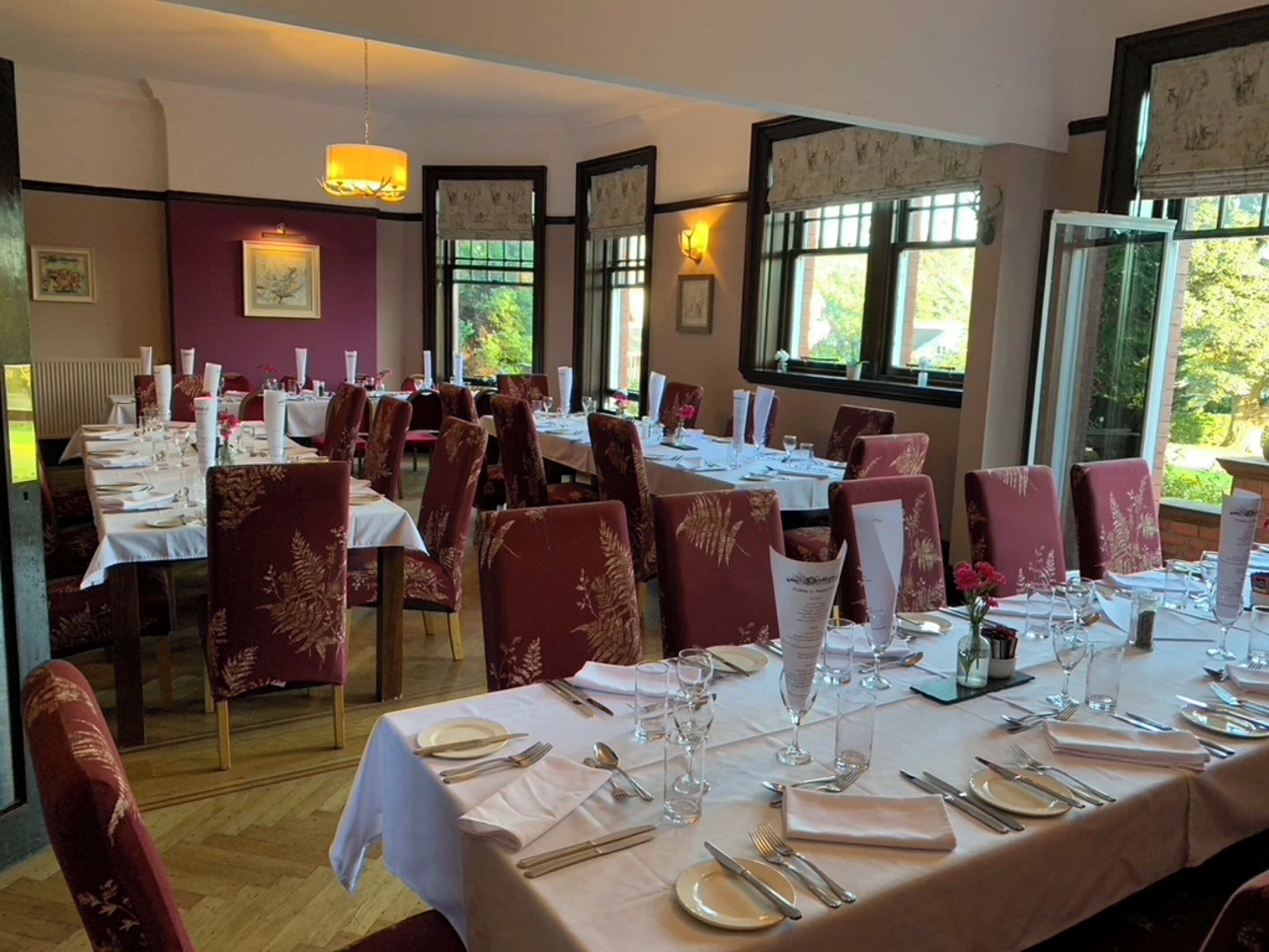 Restaurante com várias mesas preparadas para refeições, apresentando um interior clássico com cadeiras estampadas e uma paleta de cores quentes.