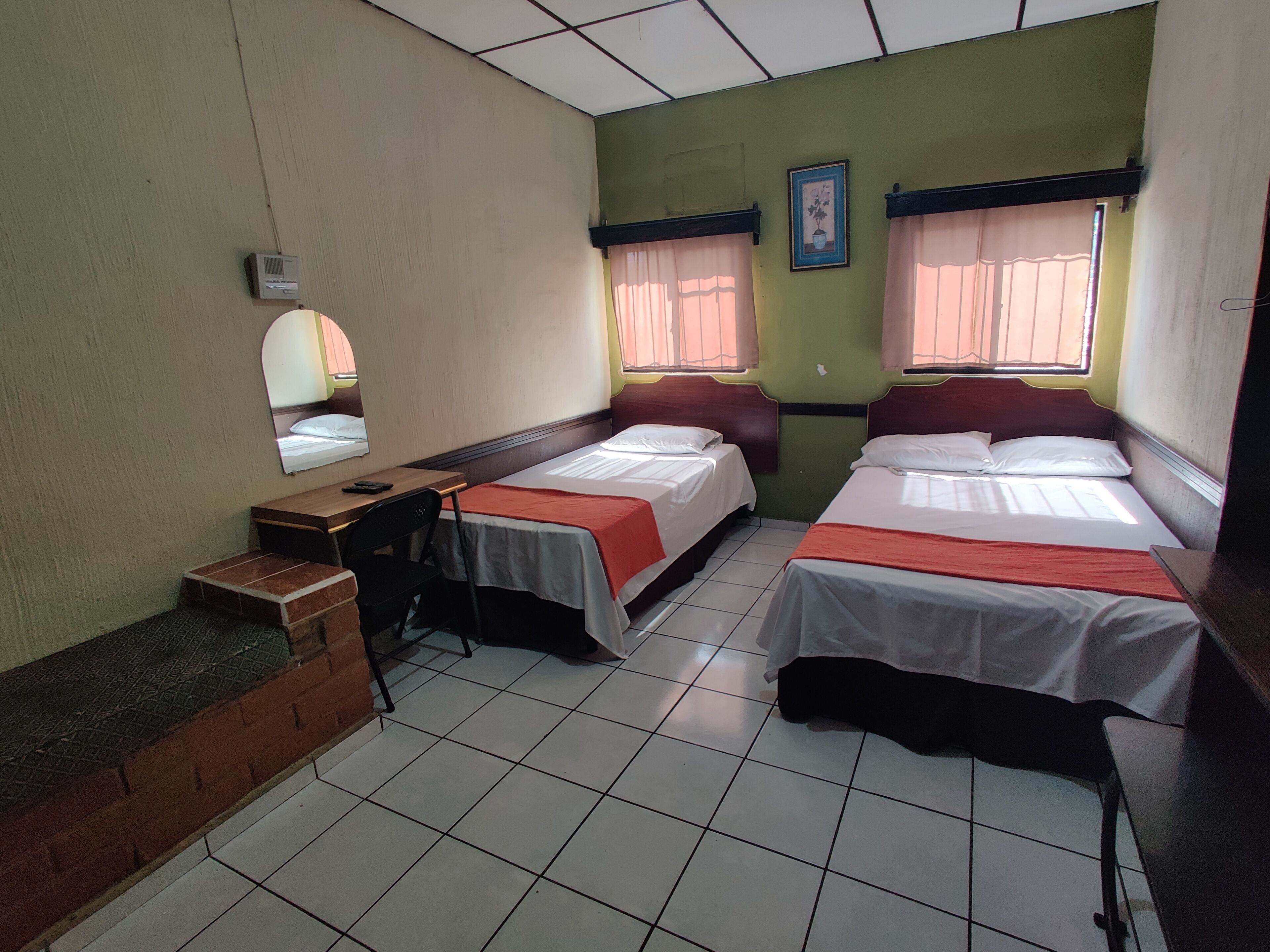 Quarto com duas camas, uma escrivaninha, uma cadeira, um espelho e uma janela com cortinas.