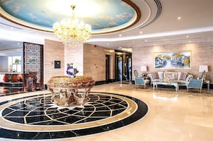 Um hall com uma mesa central ornamentada, um candelabro, um conjunto de sofás e um quadro na parede.