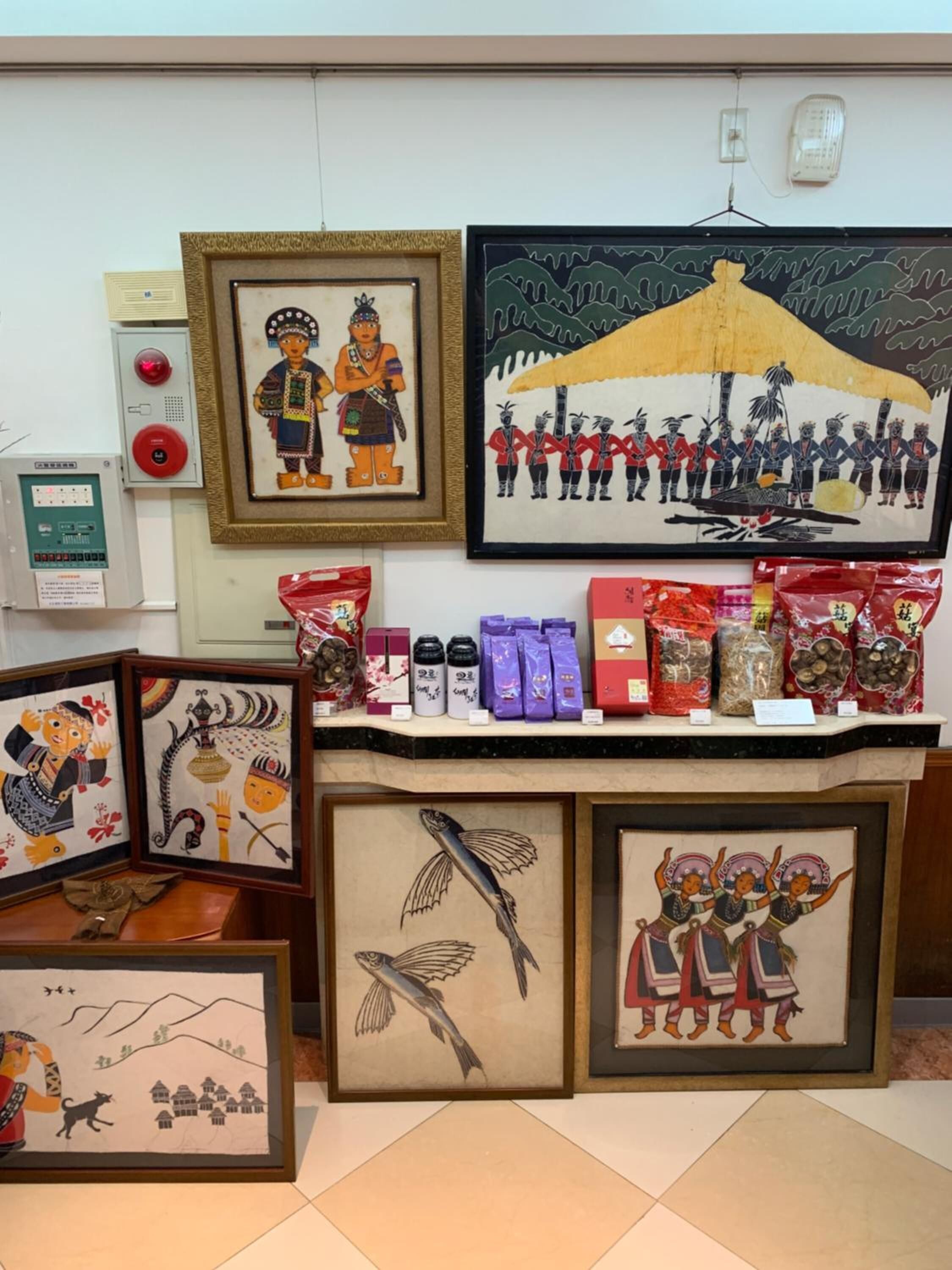 Exposição de obras de arte emolduradas e objetos culturais, incluindo figuras tradicionais e uma representação de um peixe.
