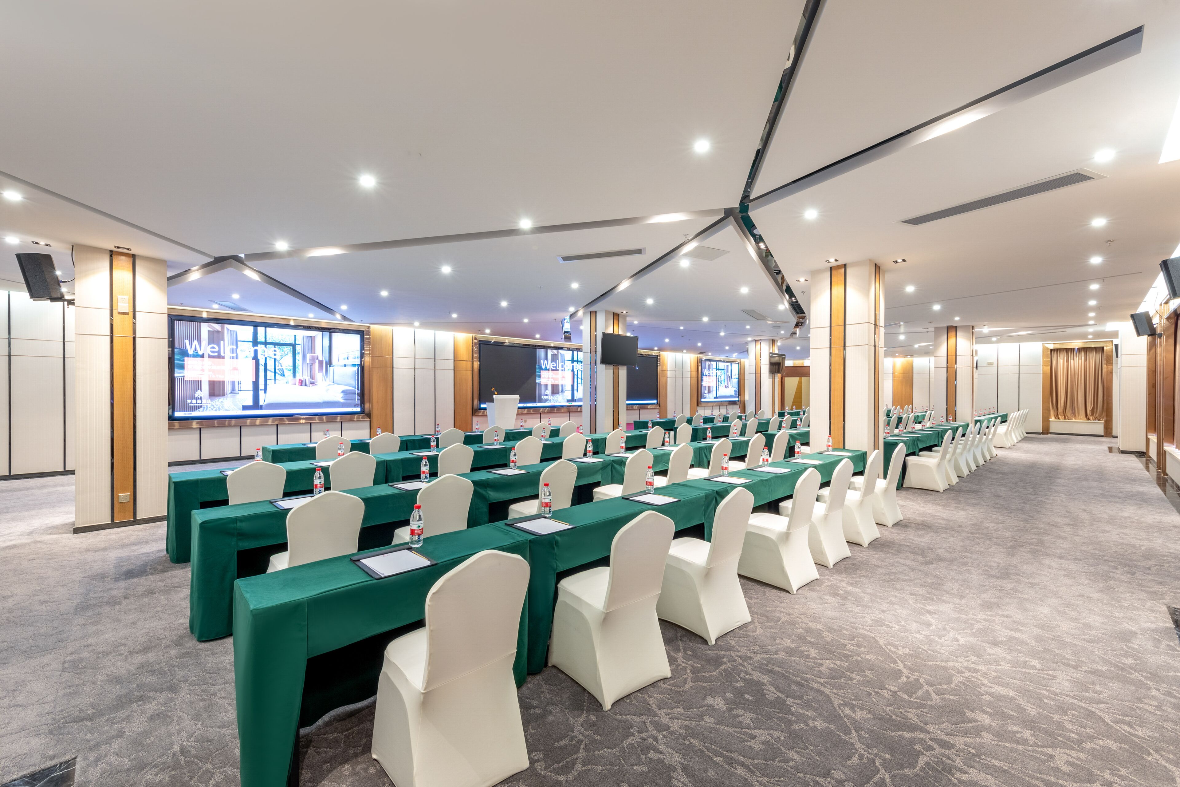 Uma sala de conferências com fileiras de mesas e cadeiras, equipada com projetores e telas.