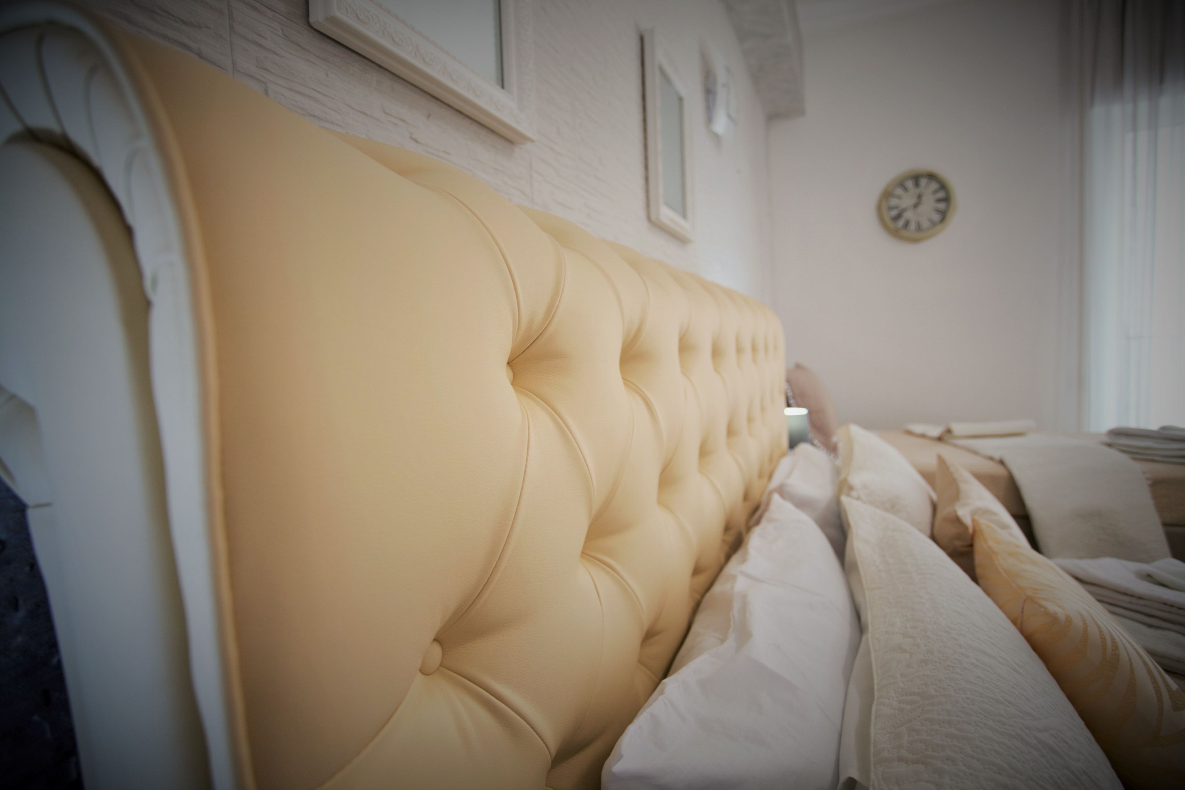 Quarto com cabeceira estofada, roupa de cama branca e um relógio na parede.