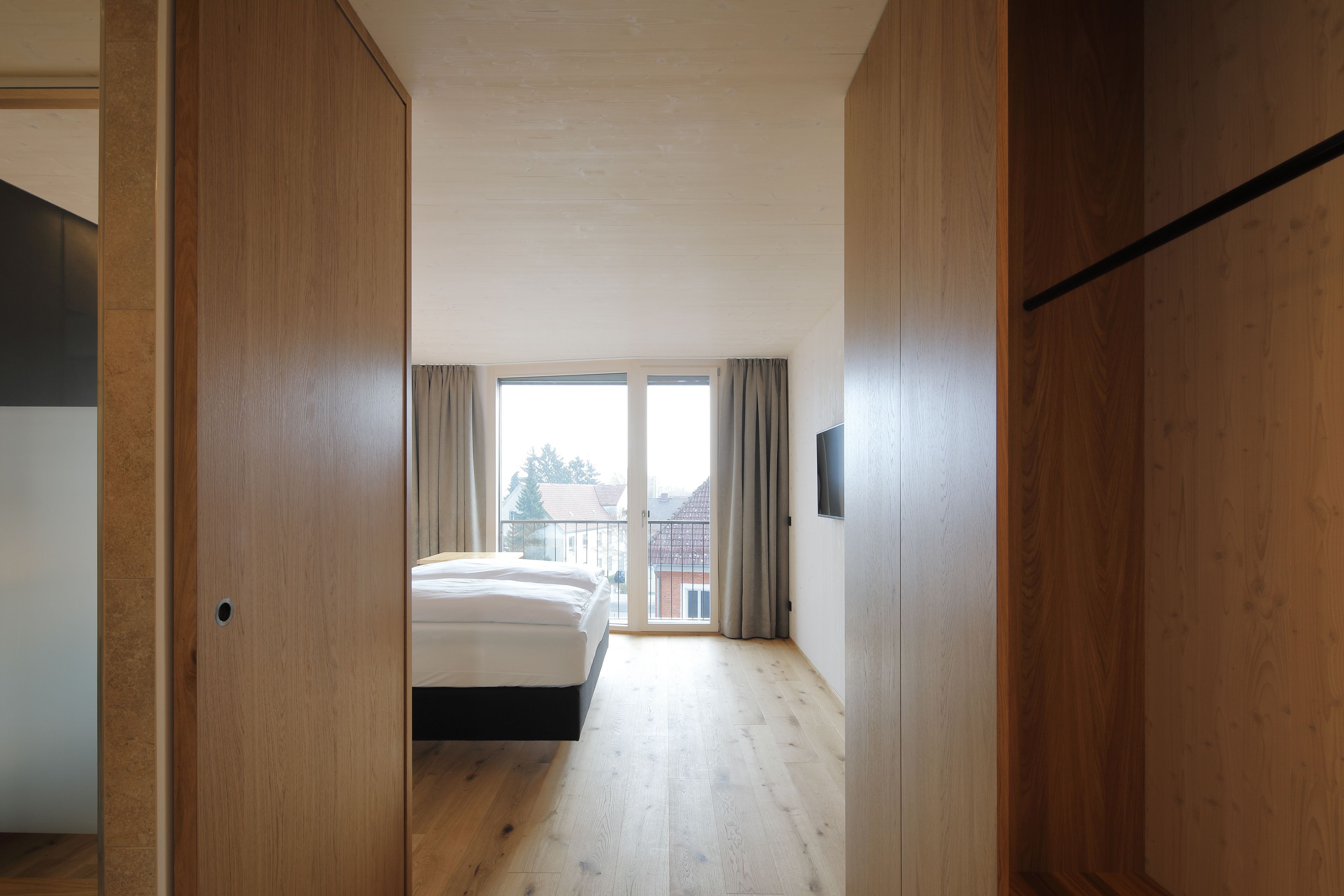 Quarto com uma cama grande, piso de madeira e vista para uma varanda externa através de uma porta de vidro.