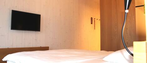 Quarto de hotel com cama, televisão montada e guarda-roupa de madeira.
