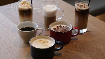 Uma mesa de madeira com quatro copos de bebidas, incluindo café e bebidas geladas, com canudos.