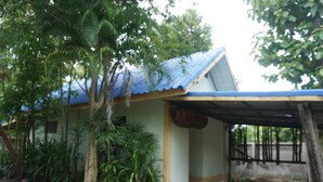 Uma pequena casa com telhado azul, rodeada por vegetação exuberante e um piso de concreto.