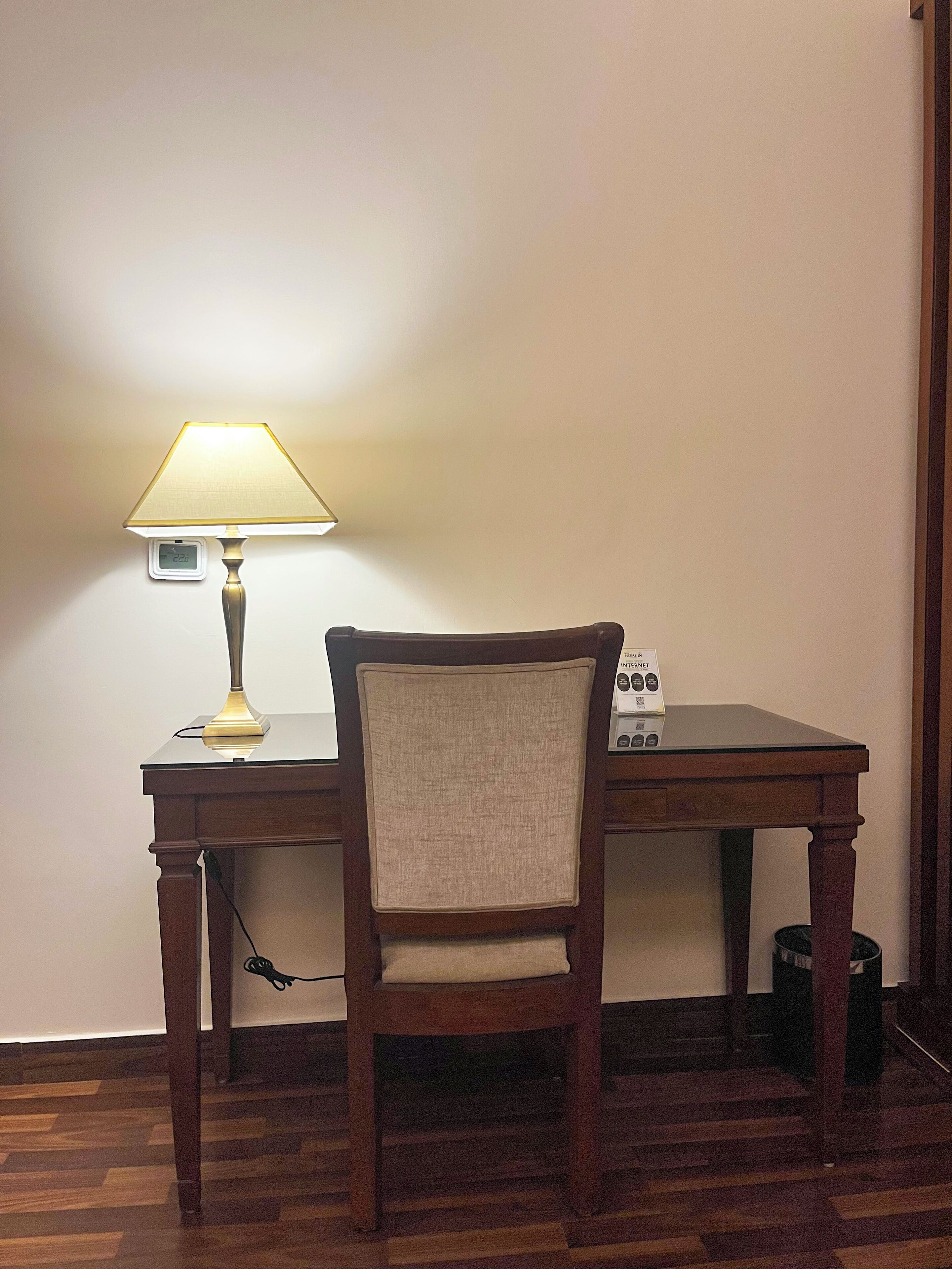 Uma cadeira de madeira com encosto acolchoado e uma mesa com luminária e régua de energia.