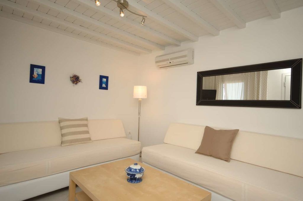 Uma sala de estar com dois sofás brancos, uma mesa de centro com um objeto azul e branco e um abajur.