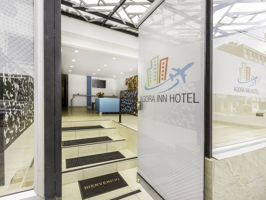 Uma área de recepção de hotel, com balcão de atendimento, bancada azul e tapete de boas-vindas.