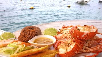 Prato de frutos do mar com arroz, um lagosta e acompanhamentos fritos sobre uma mesa à beira-mar.