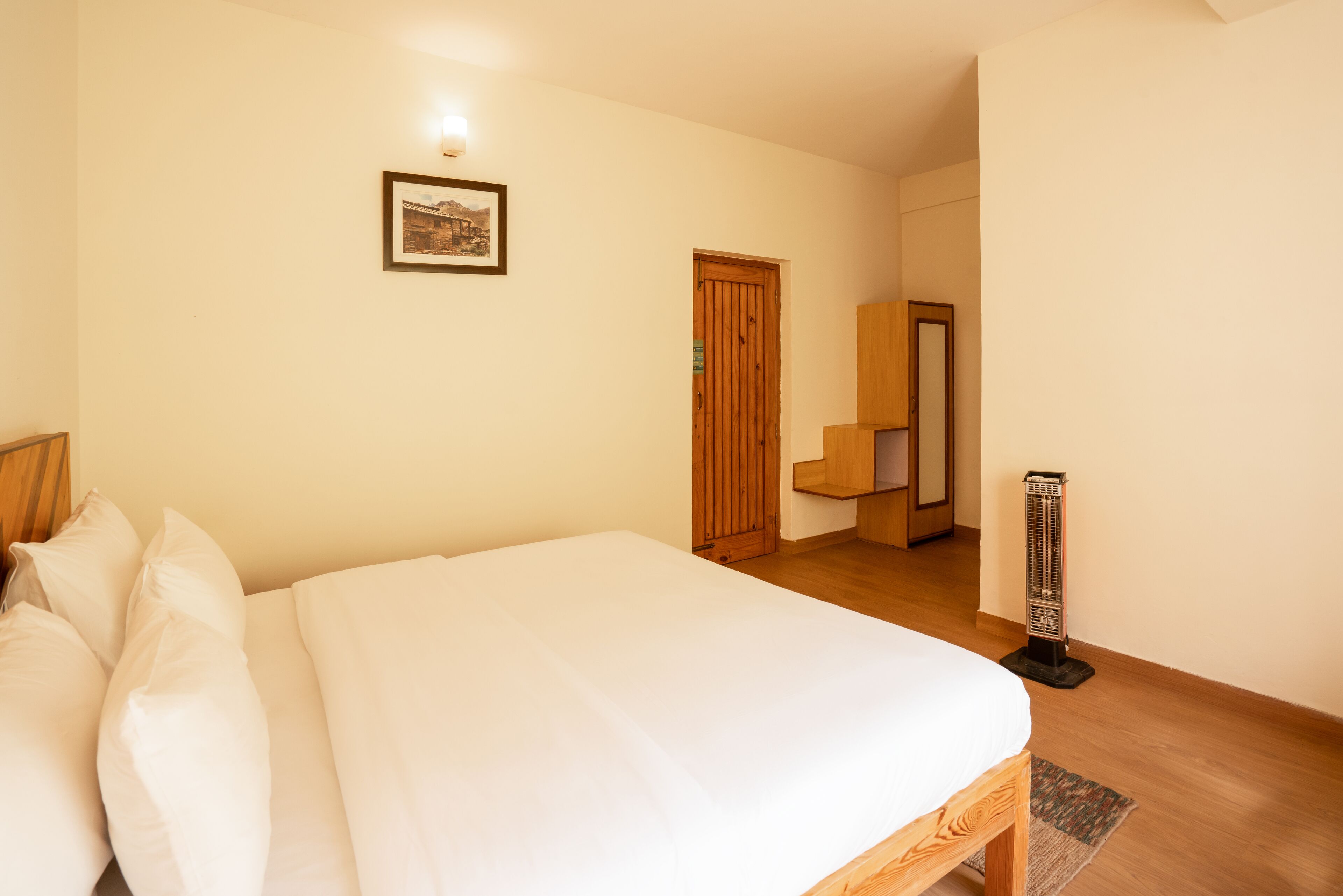 Quarto com cama, porta de madeira, espelho e aquecedor.
