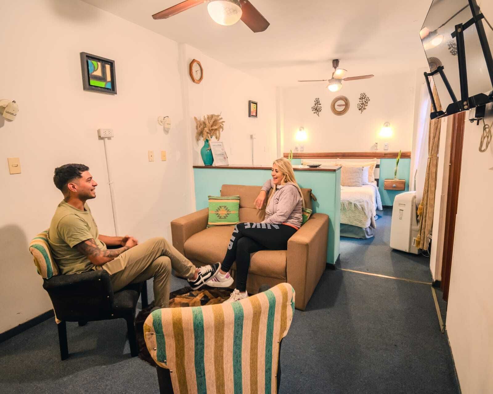 Quarto com sofá, poltrona listrada, cama, ventoinha no teto e relógio de parede.