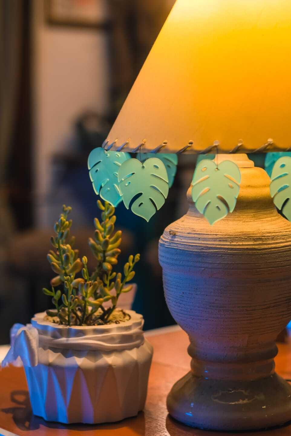 Uma luminária com padrão de folhagem decorativa, um pequeno vaso de planta e um vaso texturizado.