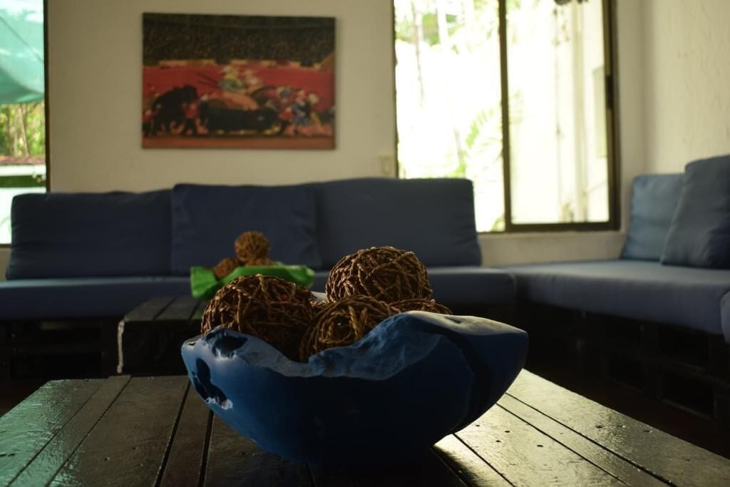 Quarto com sofá azul, mesa com uma tigela azul contendo objetos e um quadro na parede.