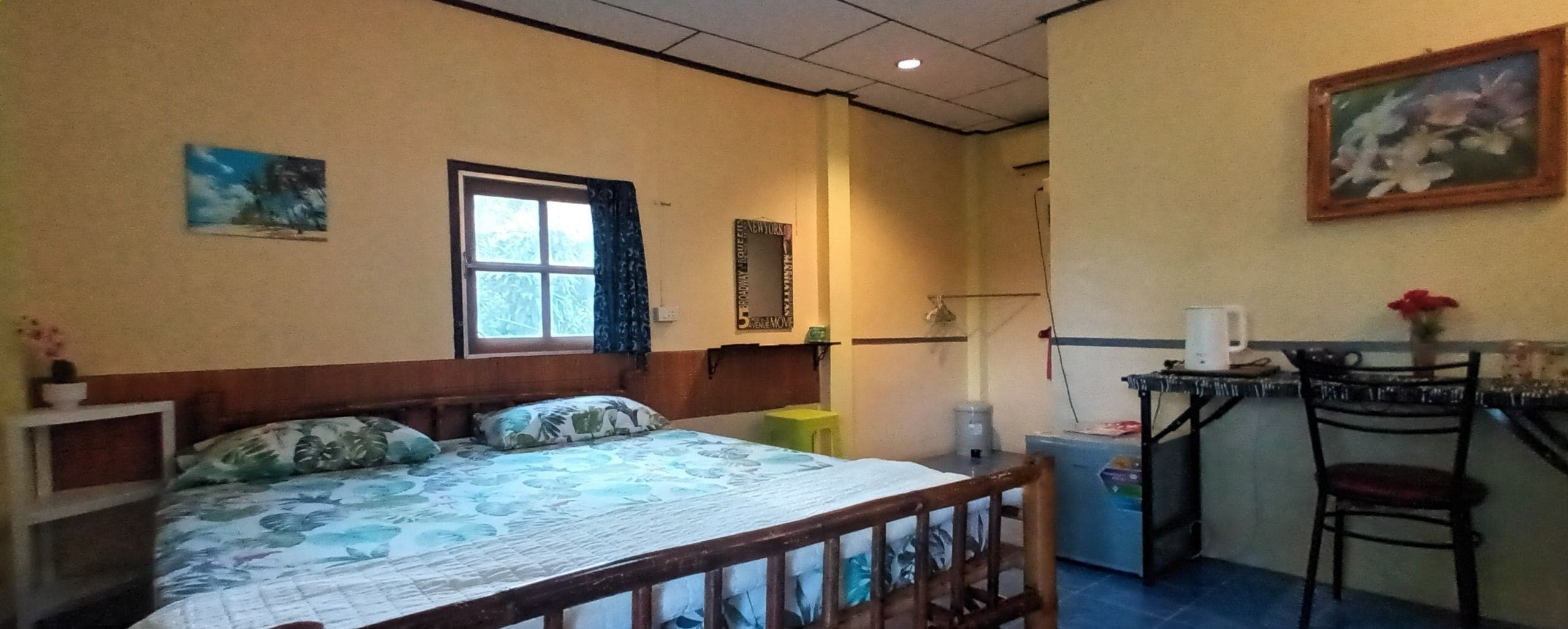 Quarto com cama, escrivaninha, cadeira, janela e pintura na parede.
