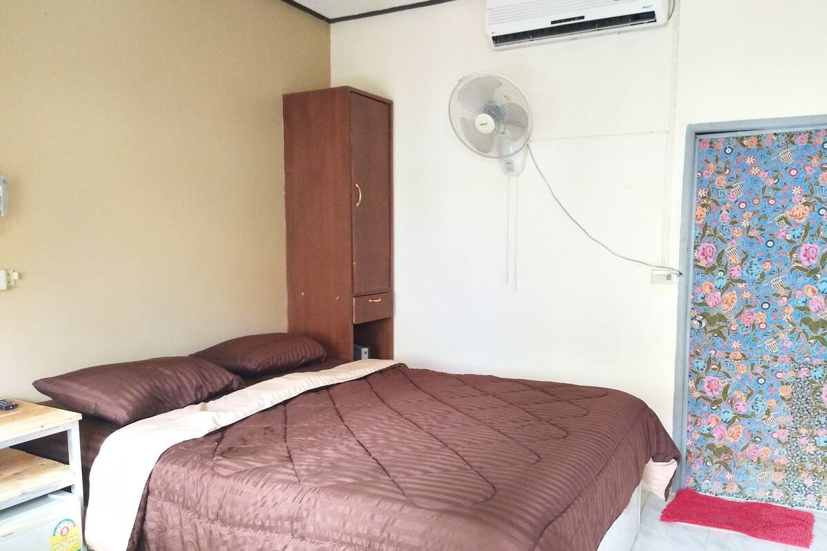 Quarto com cama, guarda-roupa, ventilador e porta com papel de parede floral.