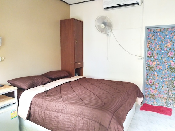 Quarto com cama, guarda-roupa, ventilador e porta com papel de parede floral.
