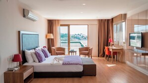 Quarto de hotel com uma cama grande, uma escrivaninha, duas cadeiras, televisão e vista para a cidade.