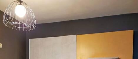 Uma cozinha moderna com micro-ondas, chaleira e pia. Há uma mesa de jantar com cadeiras e uma luminária pendente.