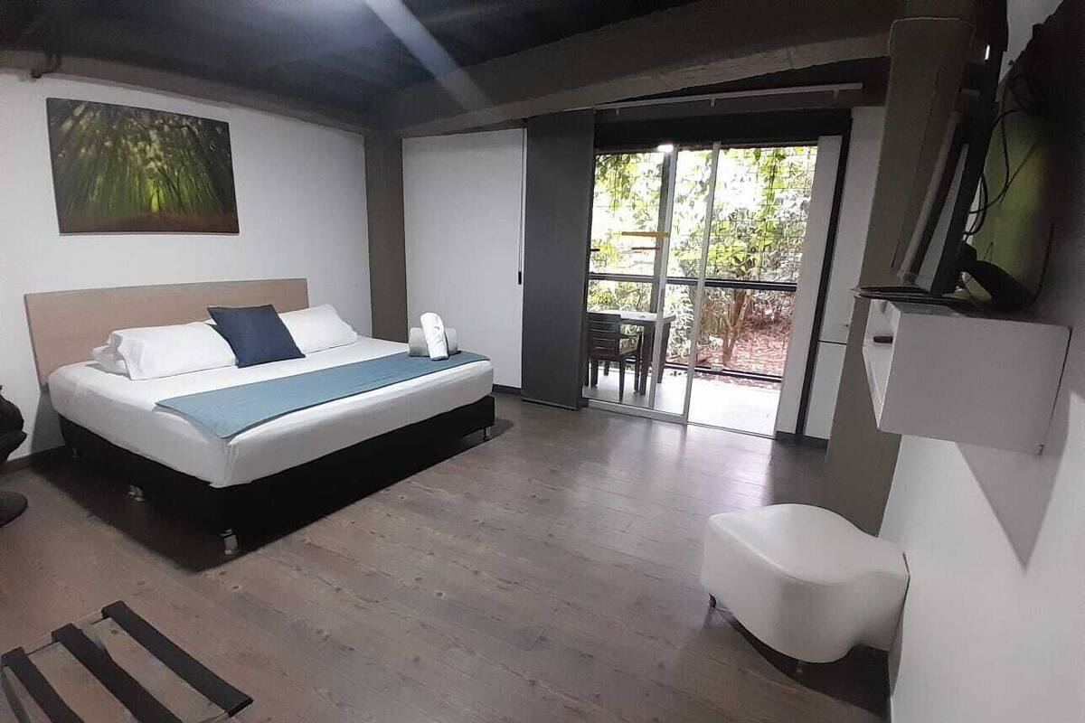 Quarto com cama, cadeira, escrivaninha, janela e porta que dá para uma varanda.