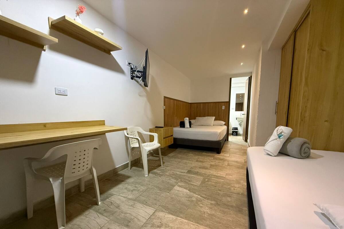 Quarto com cama, escrivaninha, cadeira, guarda-roupa de madeira e zona de chuveiro.