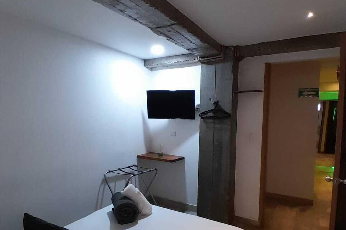 Quarto com cama, televisão presa na parede, uma mesinha e porta que dá para outro espaço.